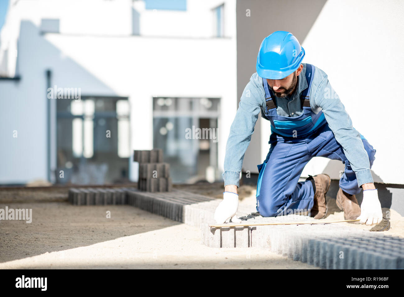 Builder in uniform laying paving tiles on the construction site with ...