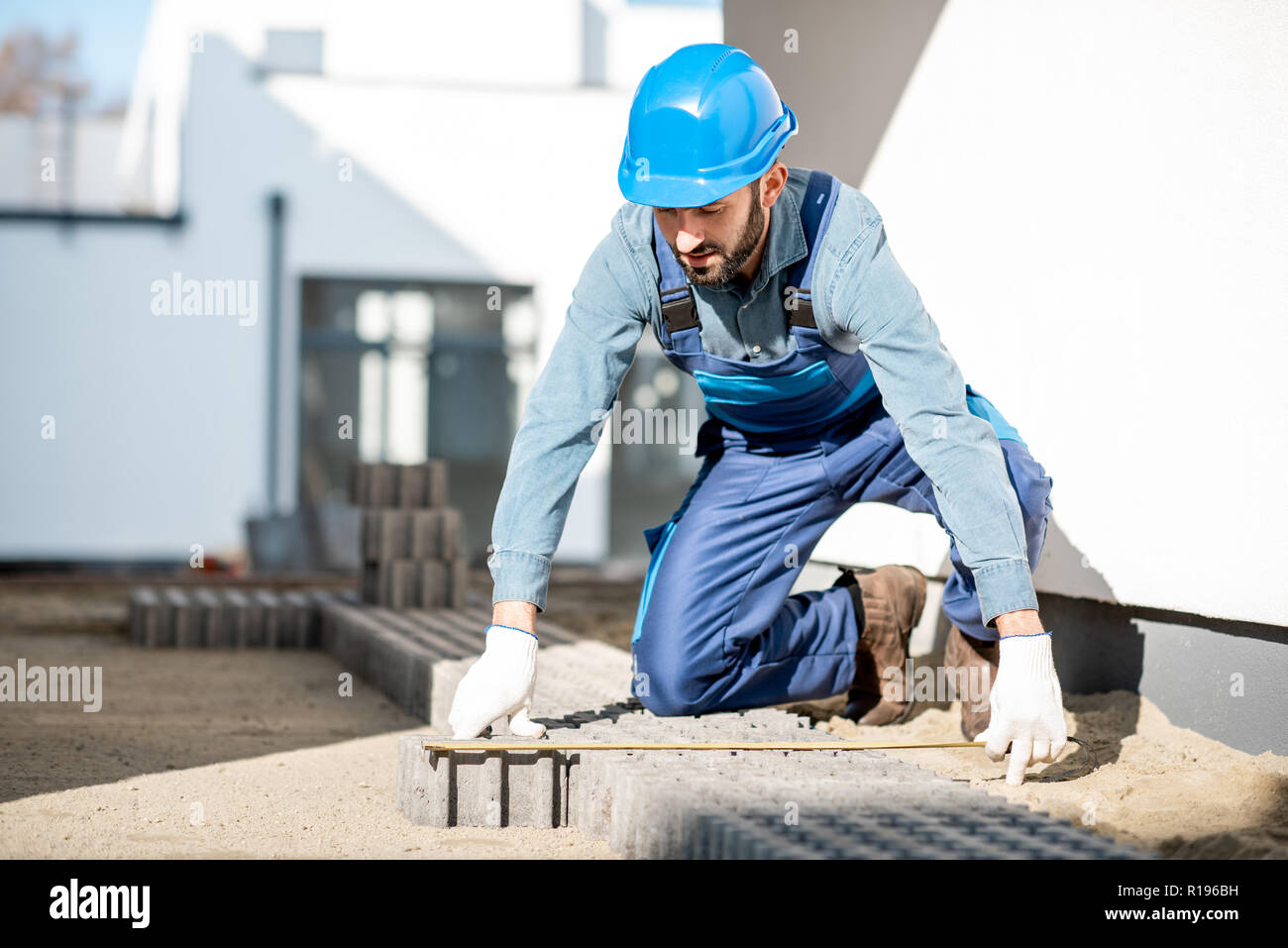 Builder in uniform laying paving tiles on the construction site with ...