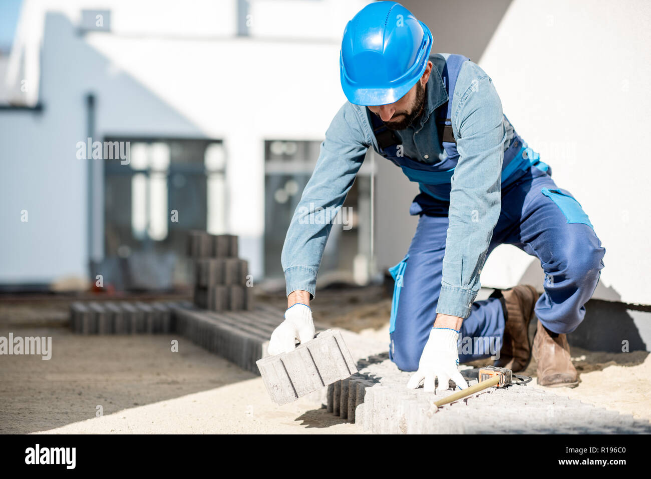 Builder in uniform laying paving tiles on the construction site with ...