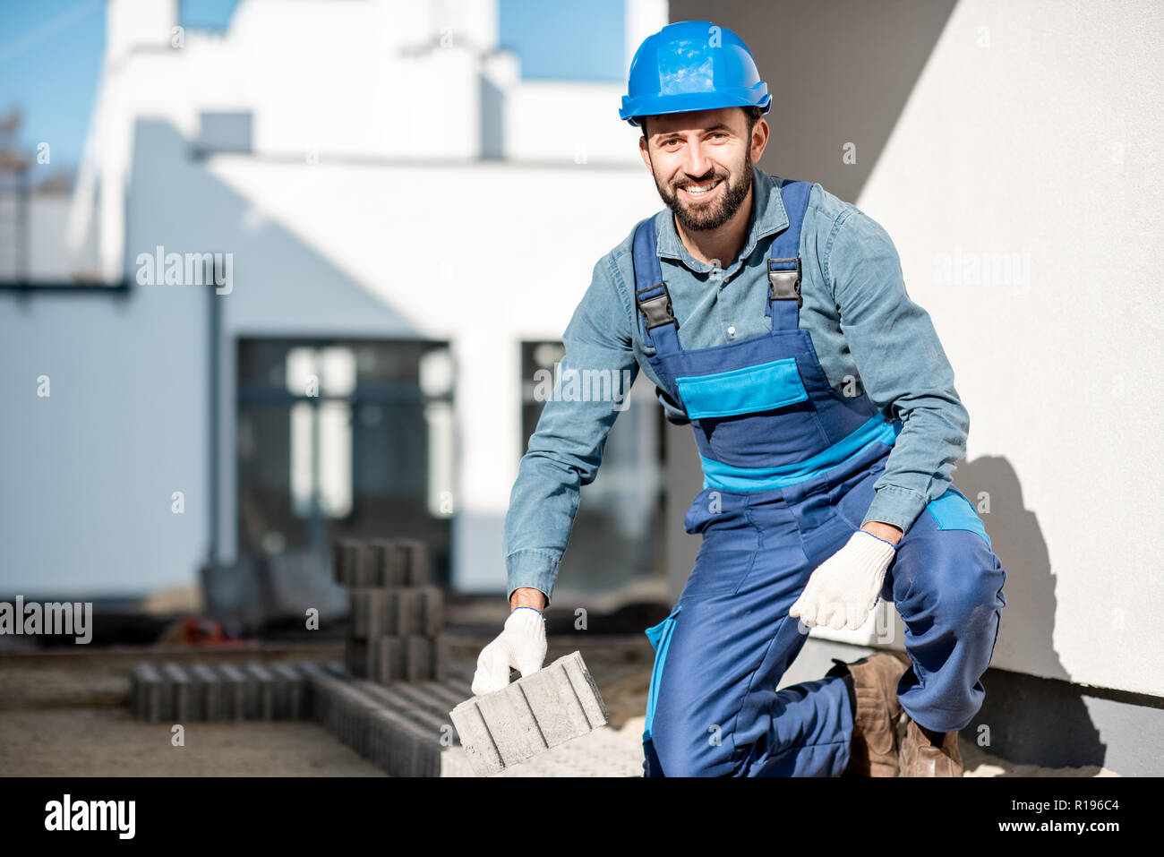 Portrait of a builder in uniform laying paving tiles on the ...