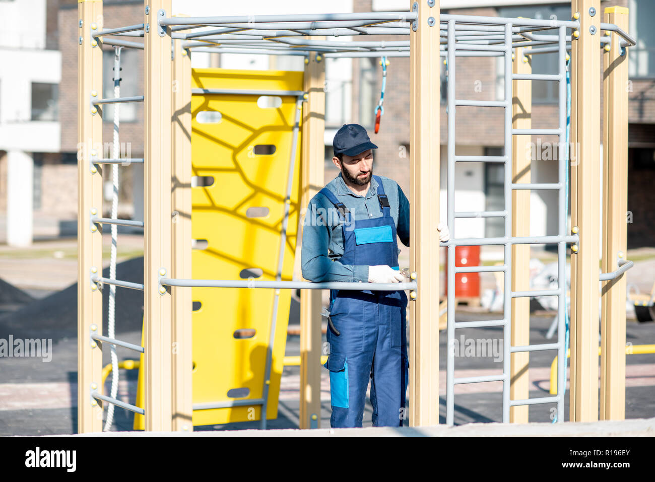 Handsome workman in uniform mounting ladder for kids playing on the ...