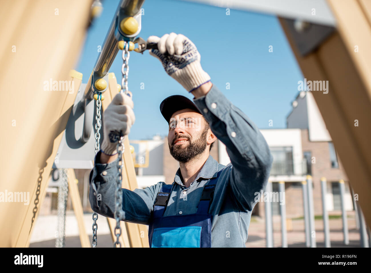 Handsome workman in uniform mounting swing on the playground outdoors ...