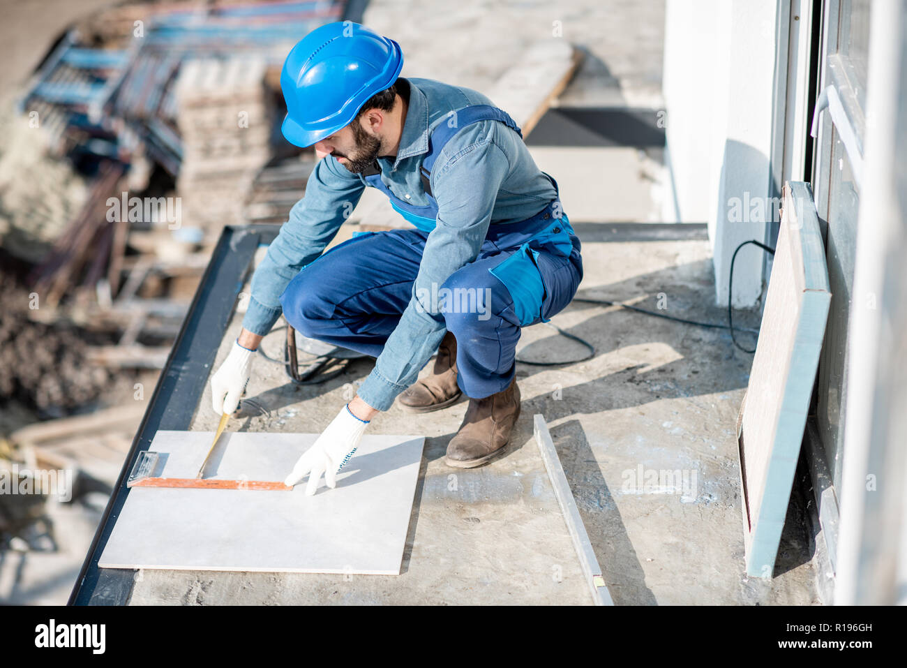 Workman in uniform mounting ceramic tiles on the balcony at the ...