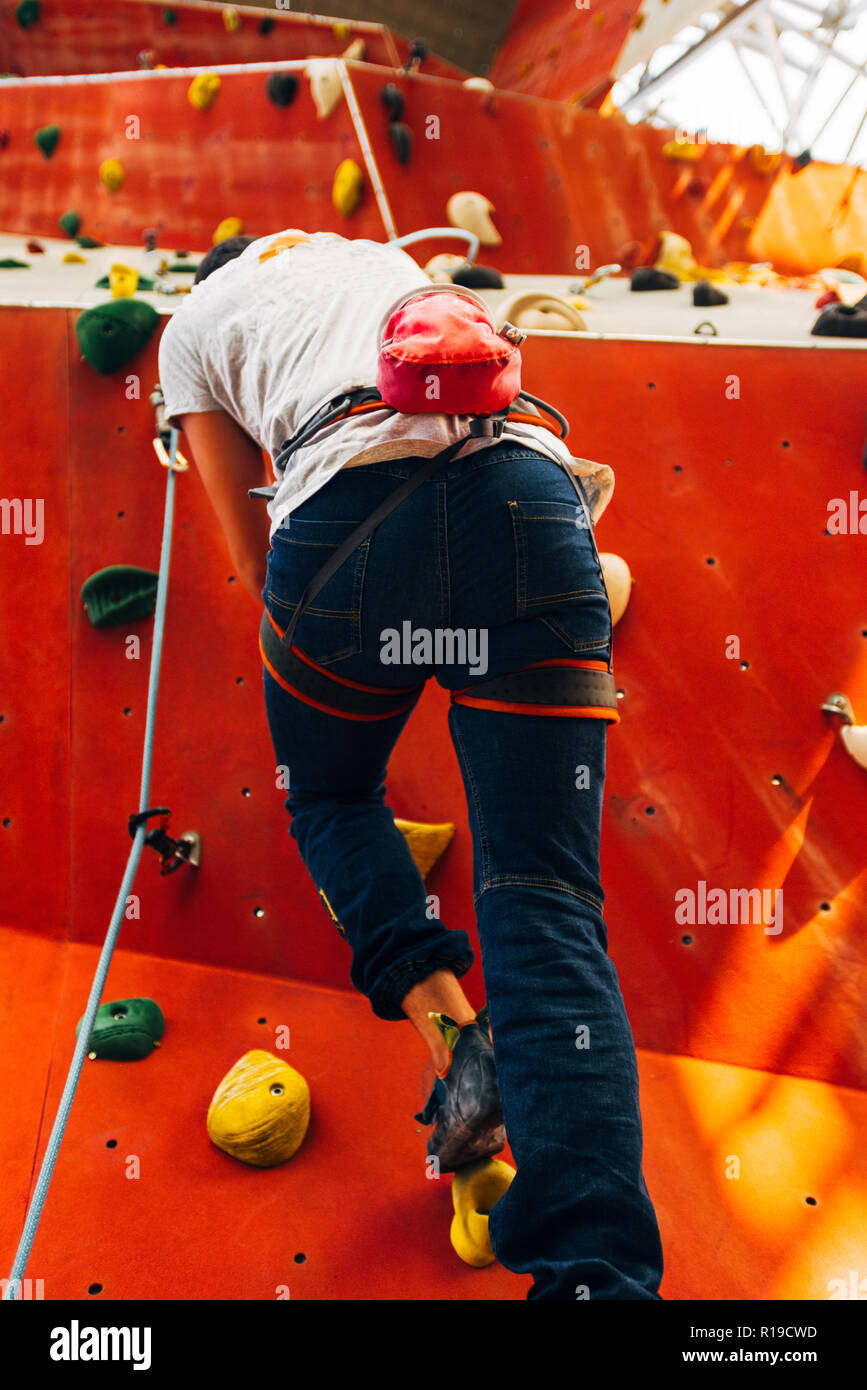 Man wearing belaying rope, climbing on a very high rock climbing wall ...