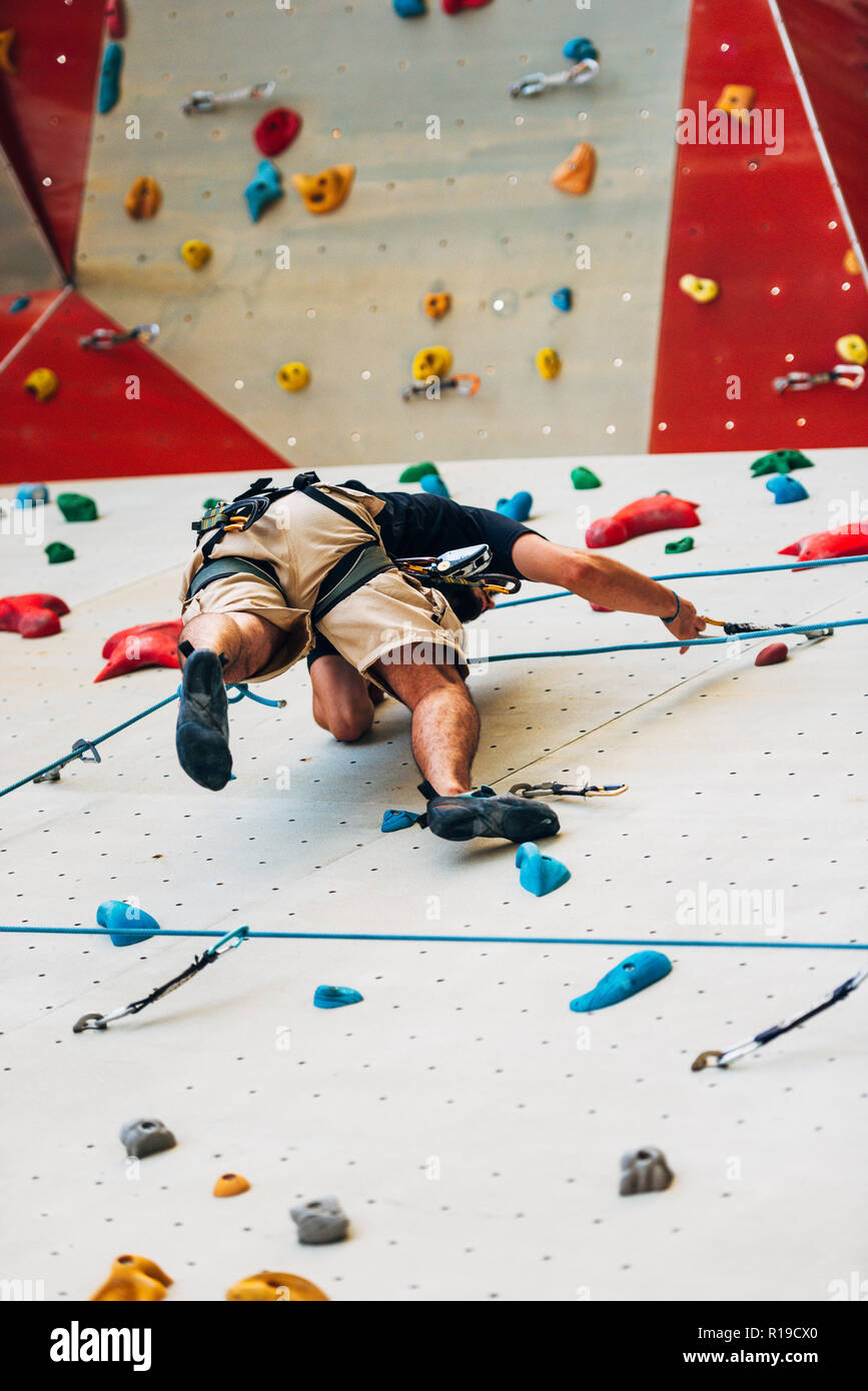 Man wearing belaying rope, climbing on a very high rock climbing wall ...