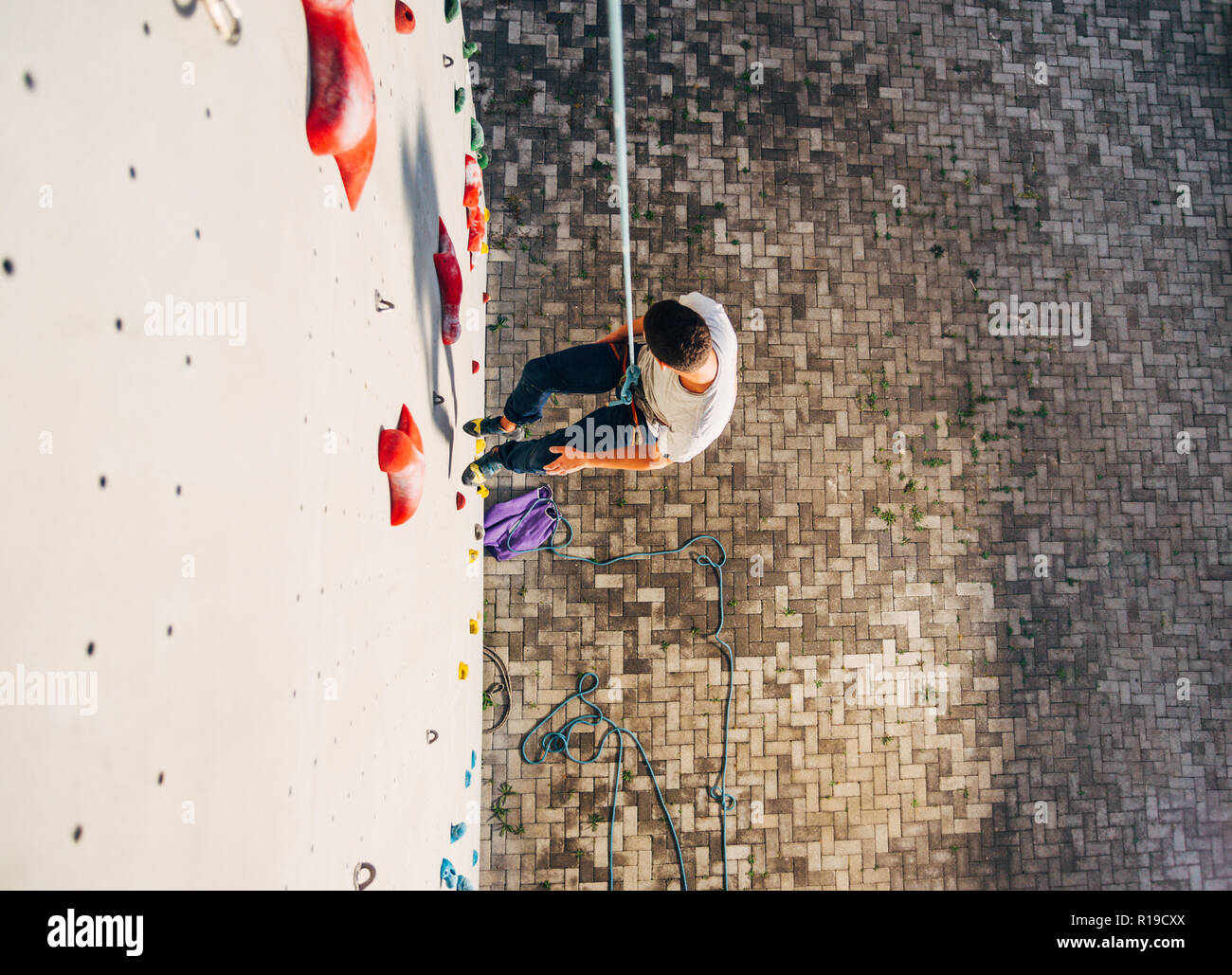 Young climber guy descending on practical rock in climbing center ...