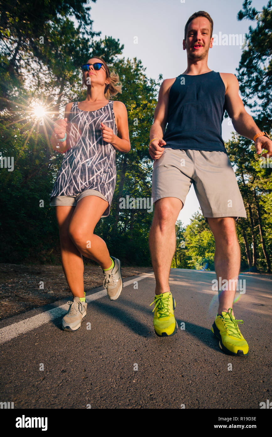 Young man and woman running through the forest road Stock Photo - Alamy