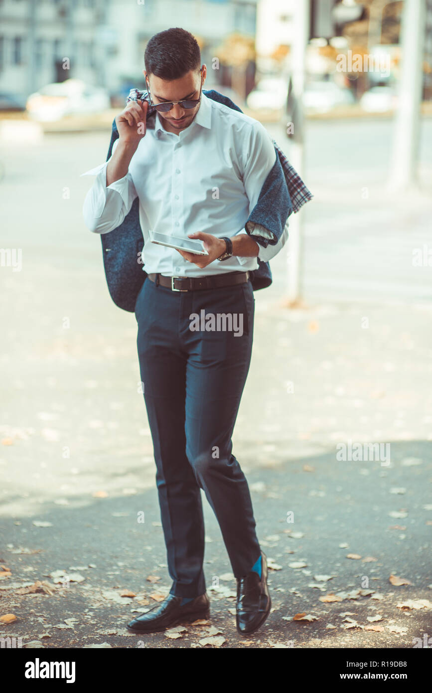 A handsome man in white shirt and grey coat is standing alone on the ...