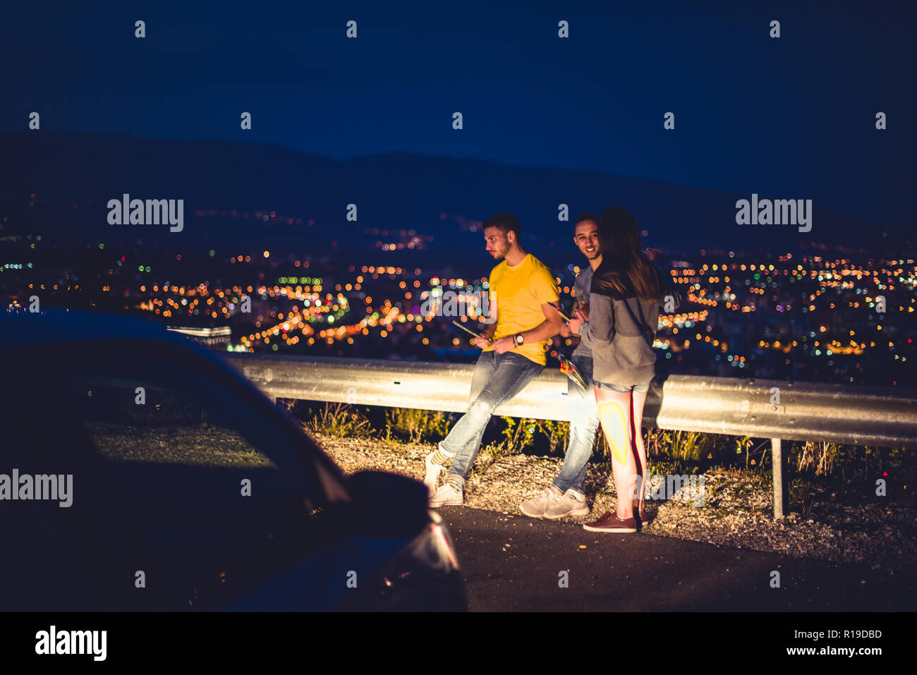 Three people at night are standing and enjoying the city panorama from ...