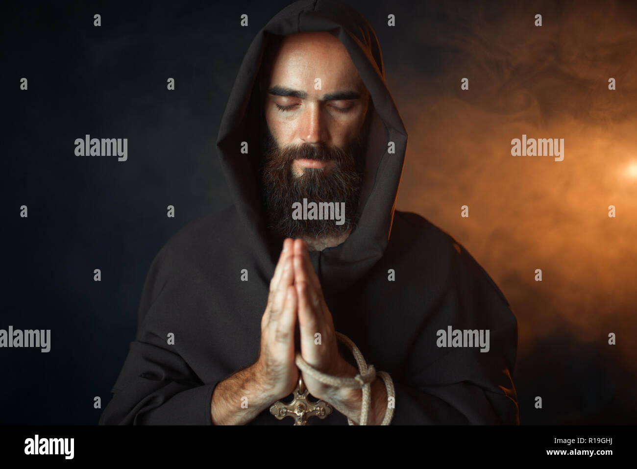 Medieval monk in black robe with hood praying with closed eyes, secret ...