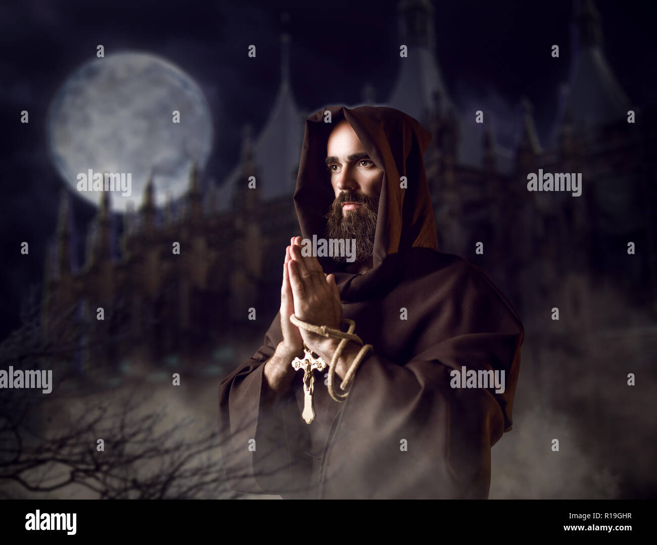 Medieval monk in black robe with hood praying against castle and full ...