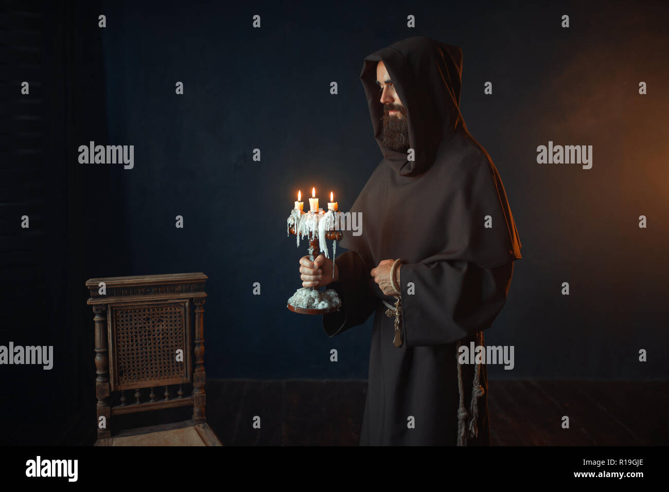 Medieval monk in robe holds a candlestick in hands, black background ...