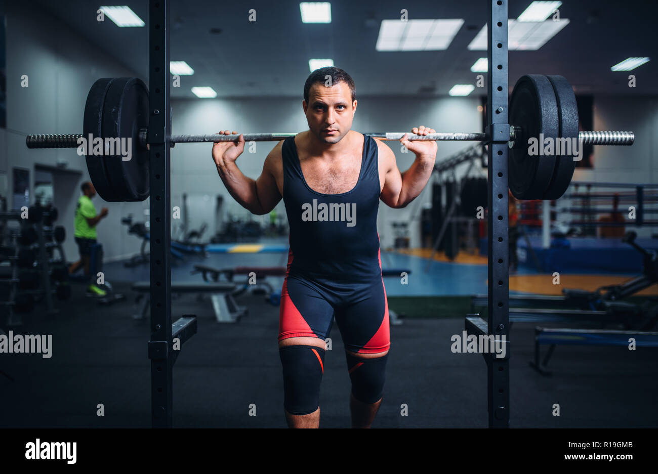 Muscular athlete in sportswear poses at the stand with barbell in gym ...