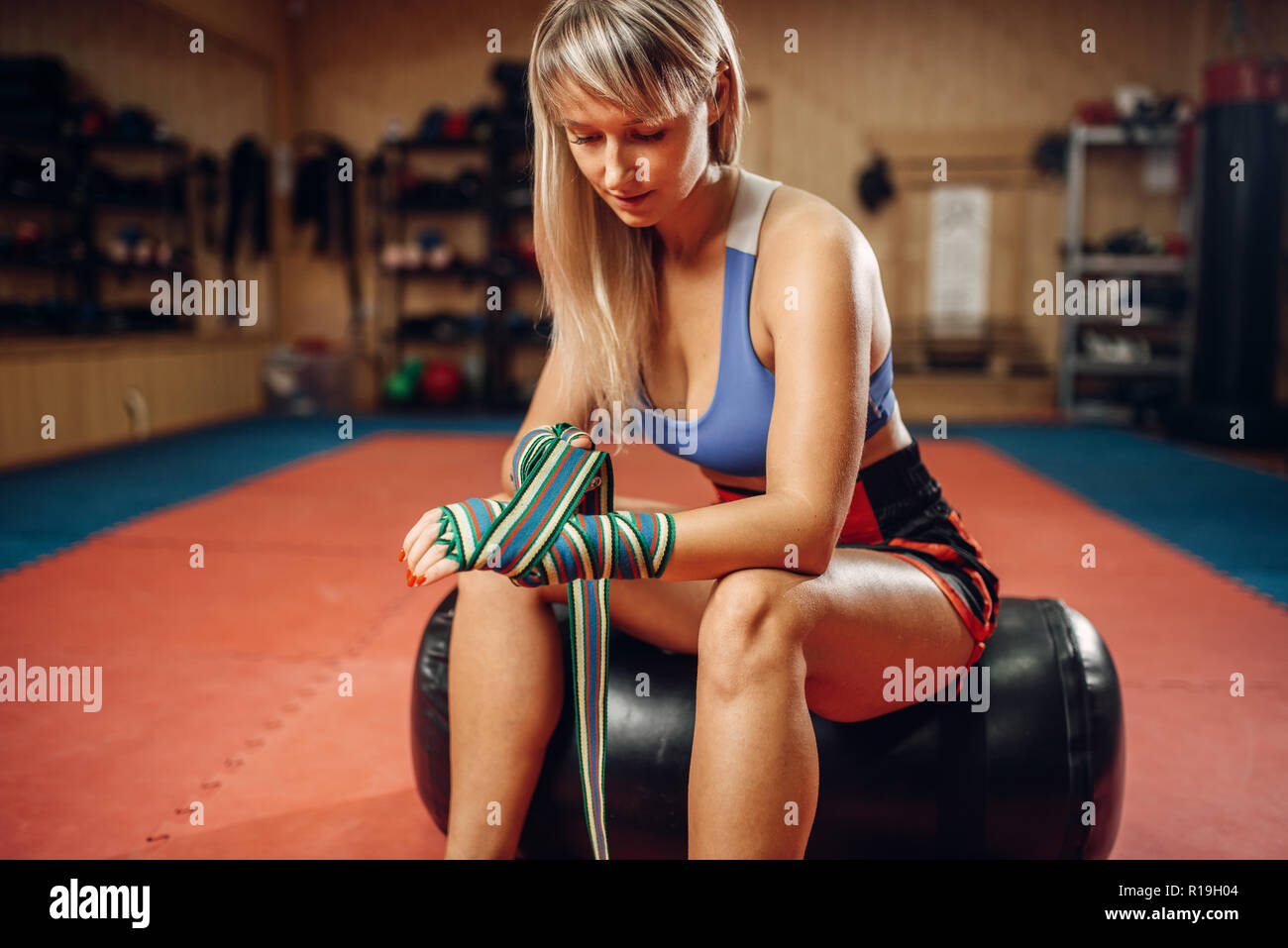 Female kickboxer in boxing bandages and sportswear sitting on punching ...