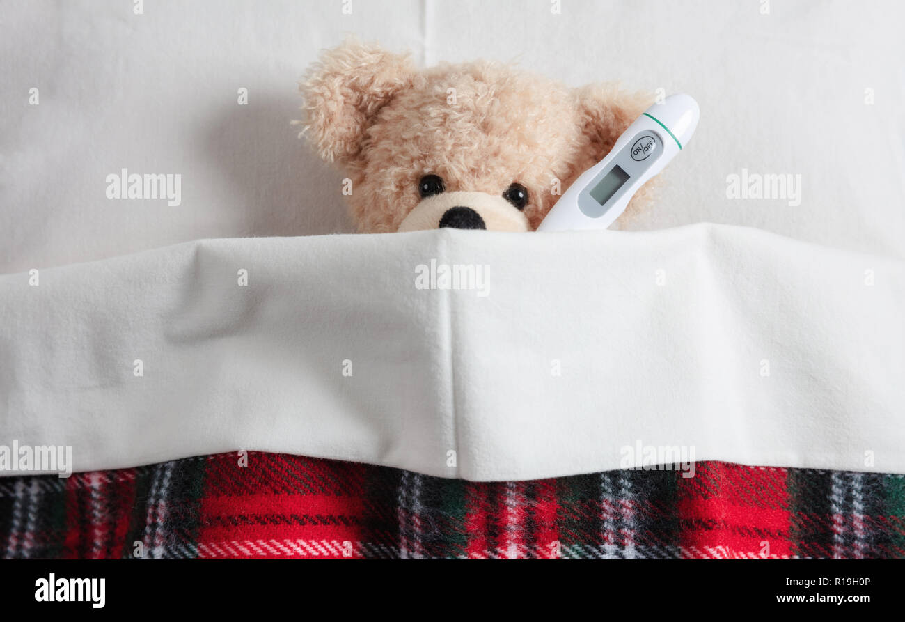 Fever, cold, flue concept. Cute teddy with a thermometer in bed ...