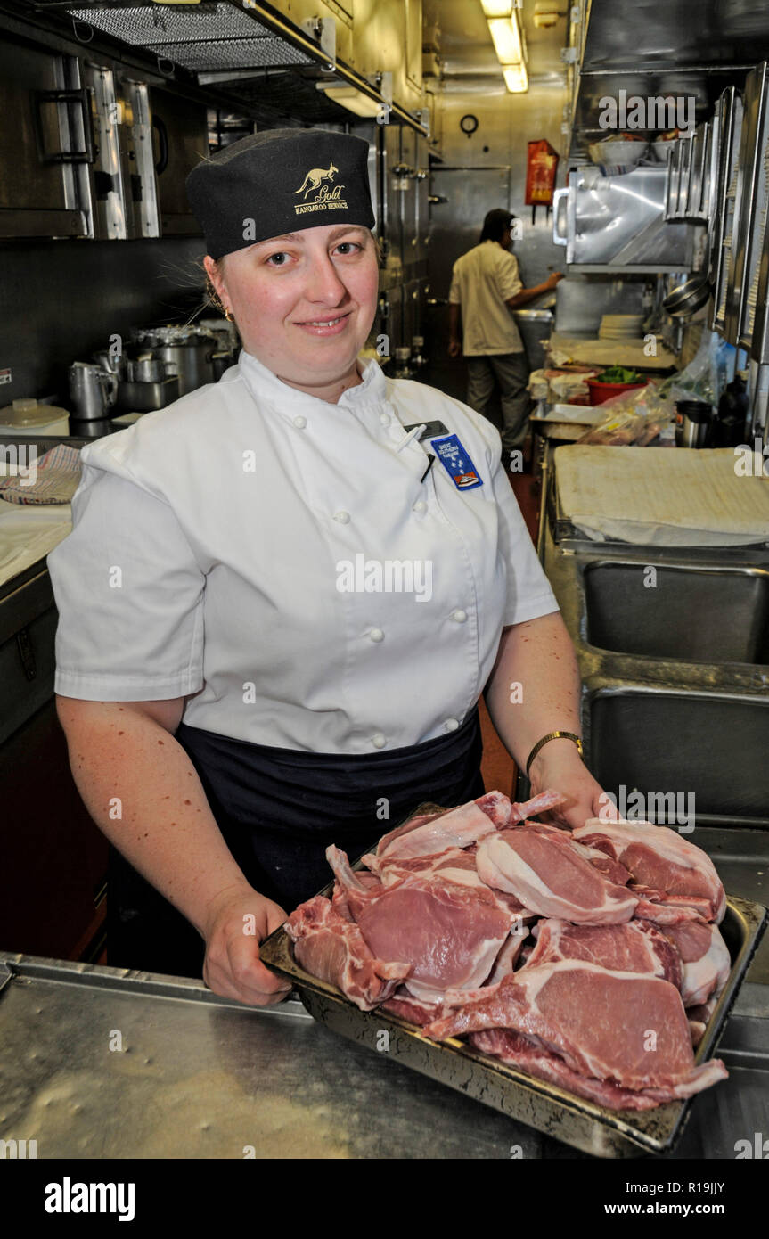 A chef holding a tray of raw meat to be cooked in the kitchen onboard ...