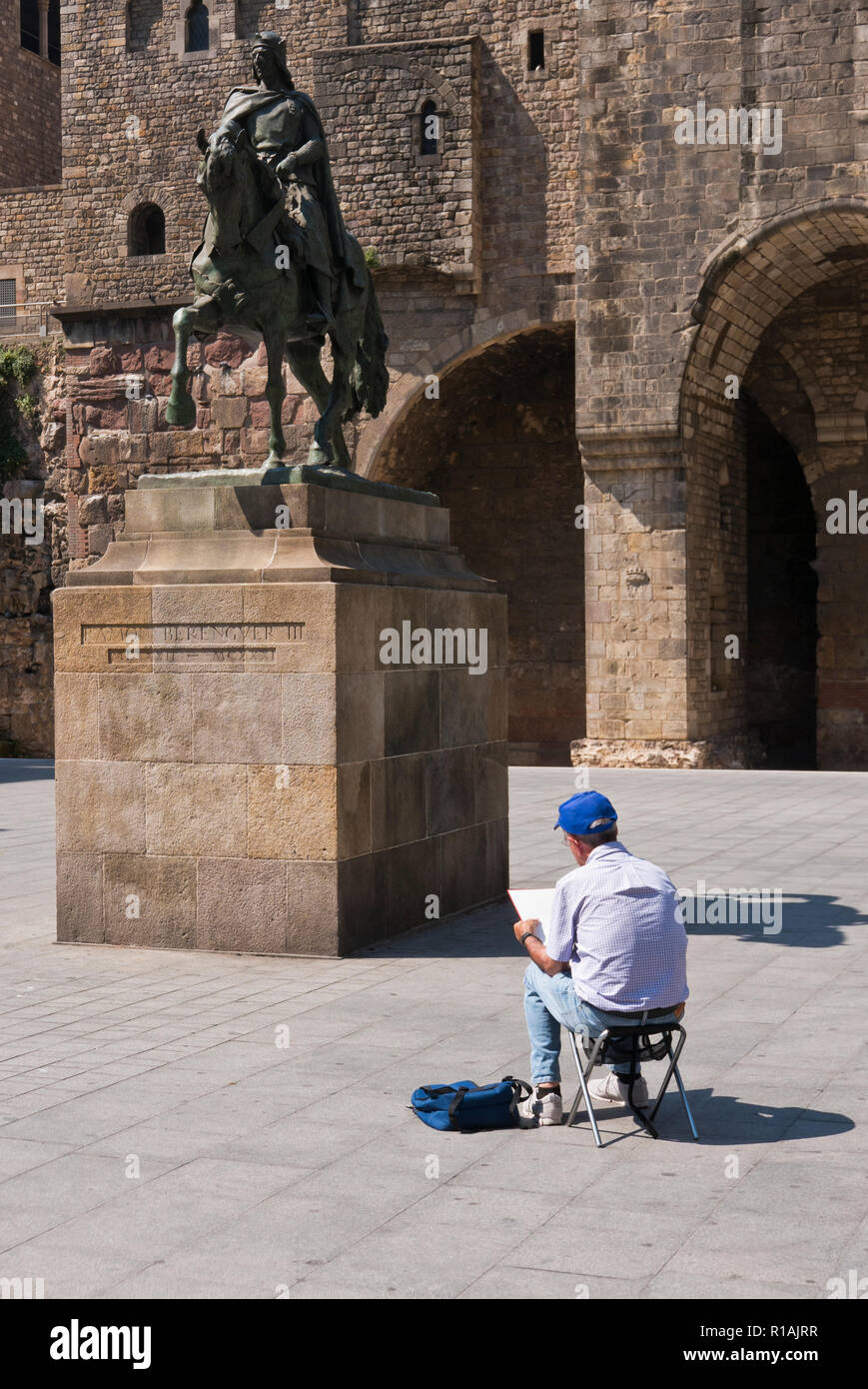 An male artist sitting on a small stool painting a statue of a man on ...