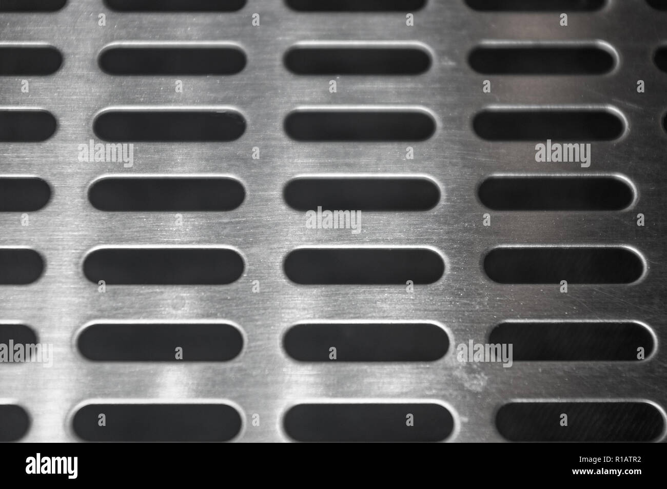 stainless steel grating with oblong holes on black background, close-up ...