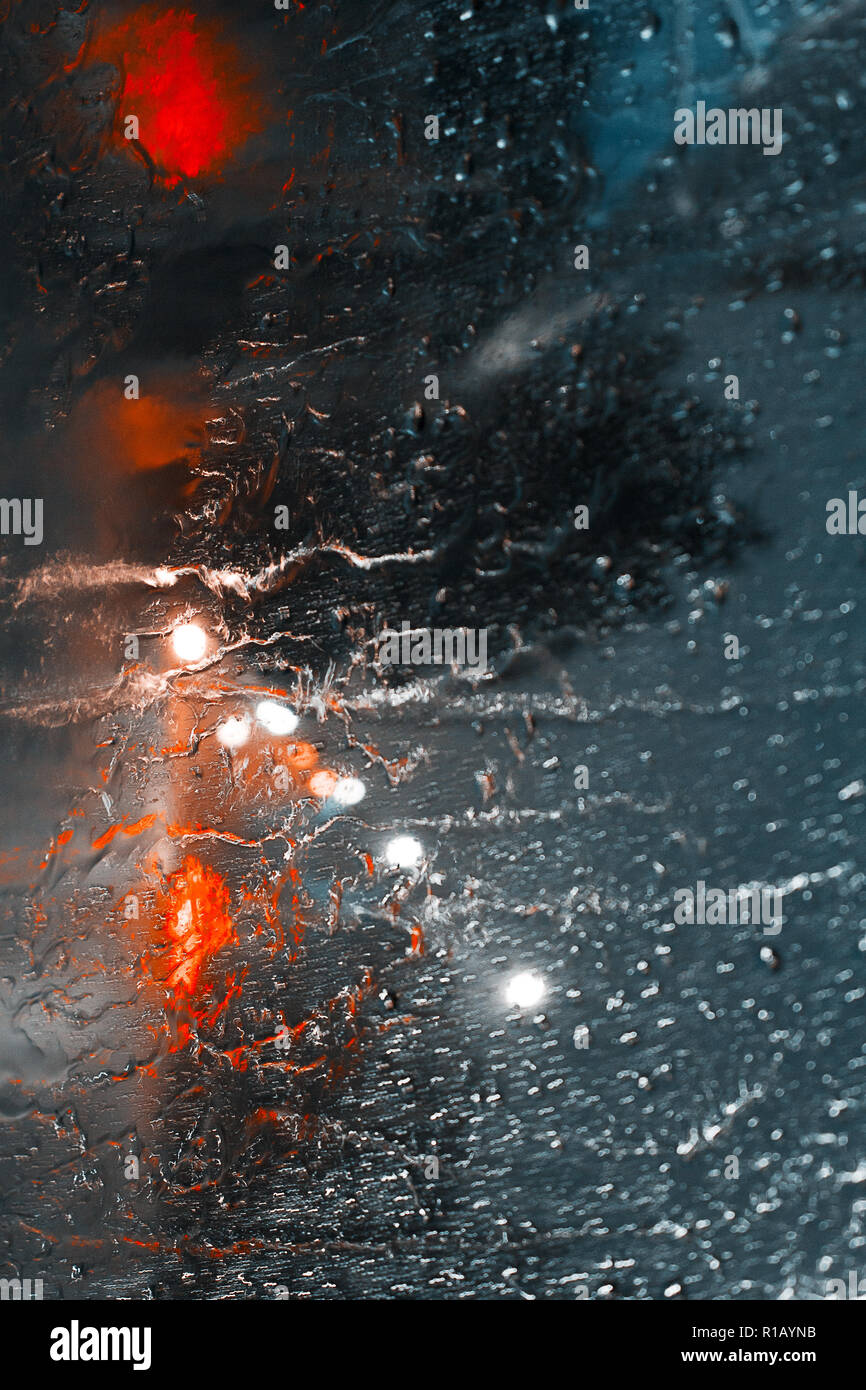 Abstract image of drops of rain on window with night reflections lights ...