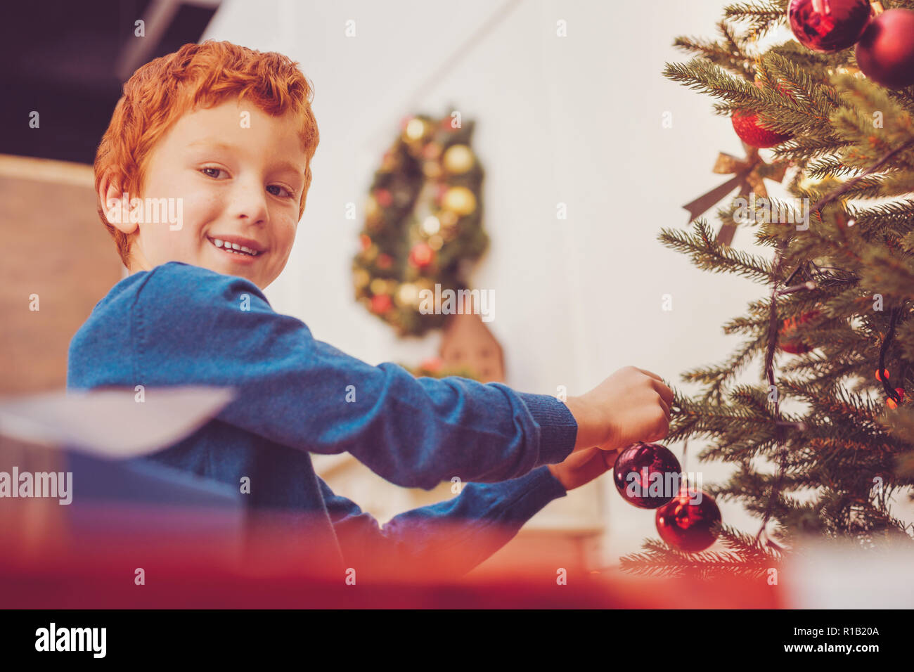 Upbeat red-haired boy posing while decorating Christmas tree Stock ...