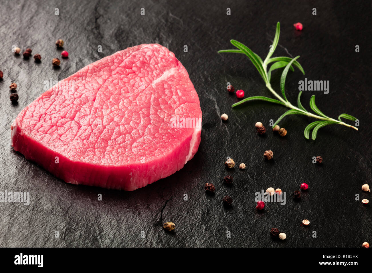 A photo of a steak of eye round beef, a raw cut, with rosemary and ...