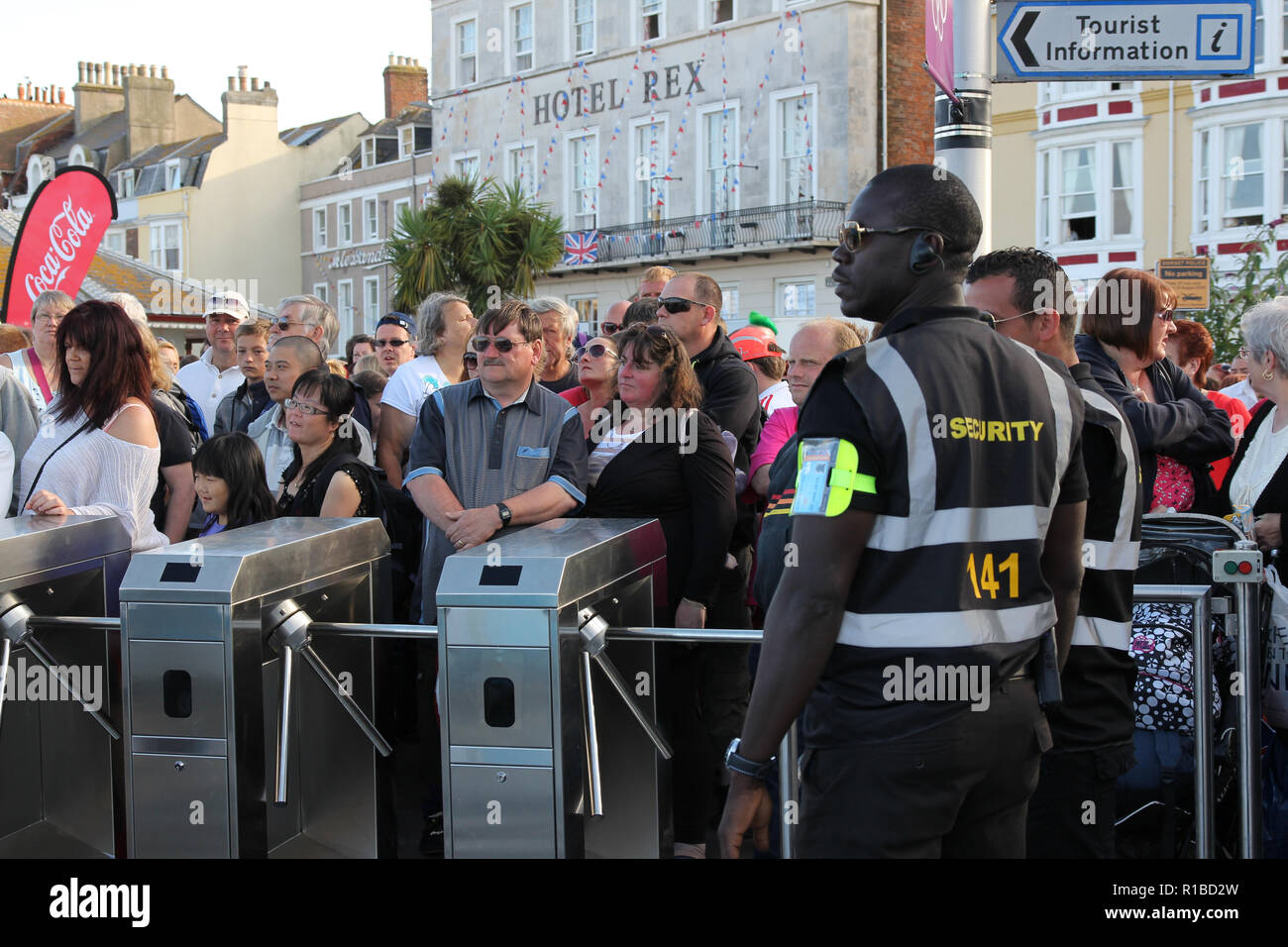 Crowds wait behind turnstile, waiting for the event to open. Watched by ...
