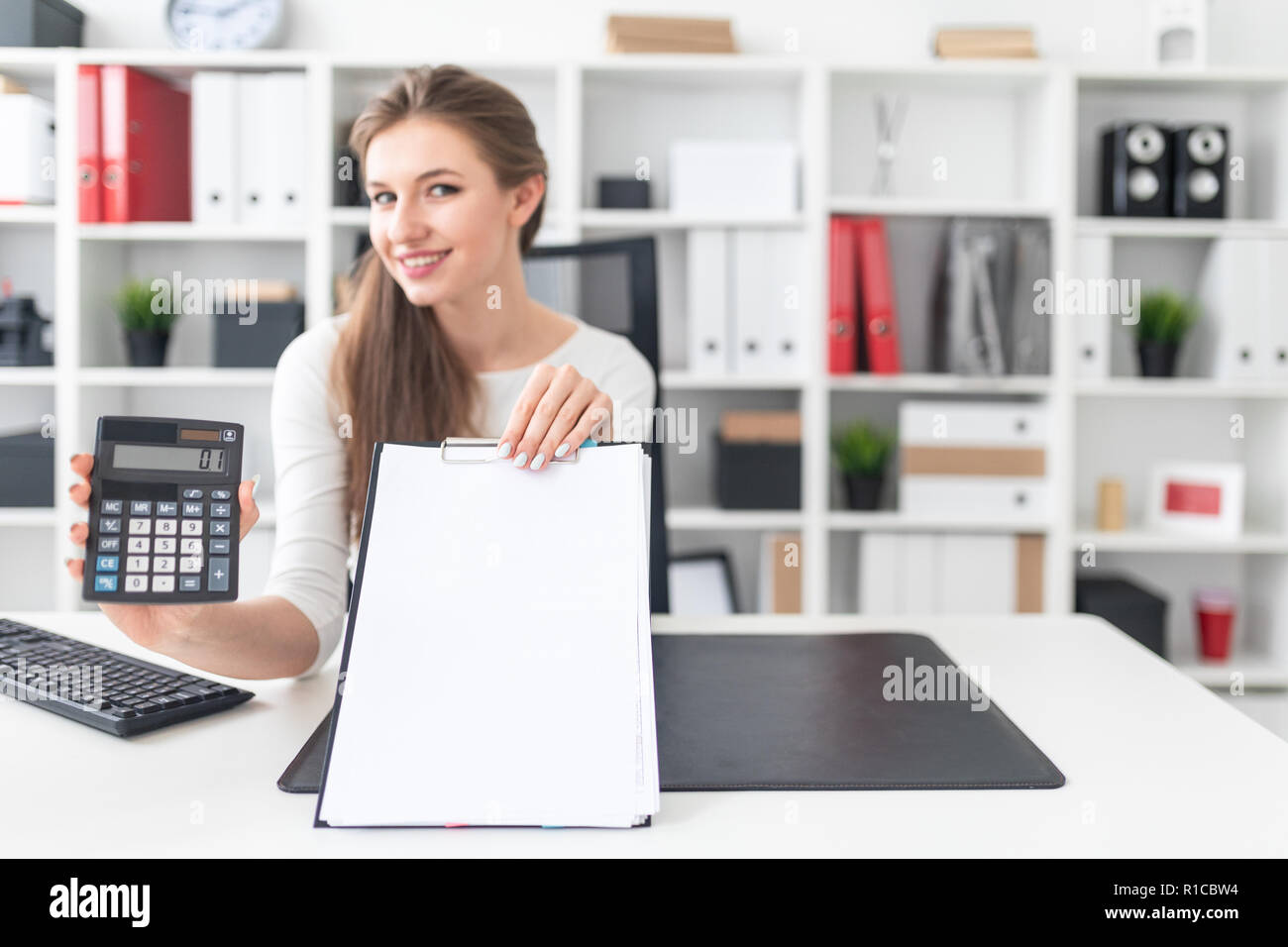 A young girl sitting at a table and holding a calculator and a blank ...