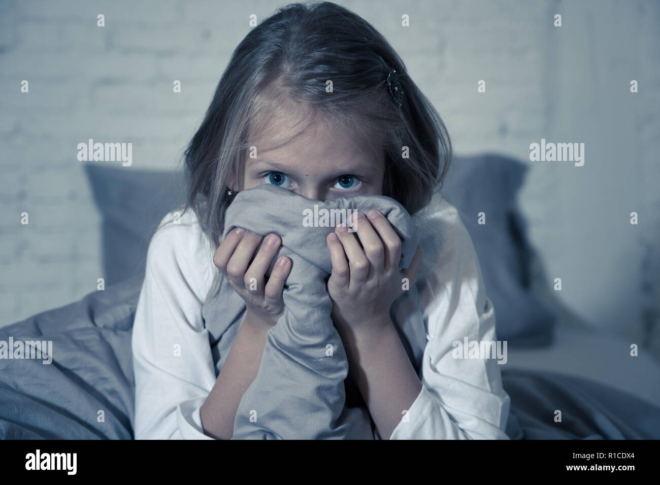 Scared little girl staying sleepless hiding behind the duvet looking ...