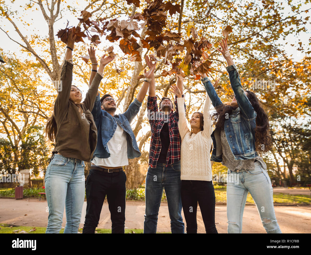 Group of friends in the park having fun throwing leaves in the air ...