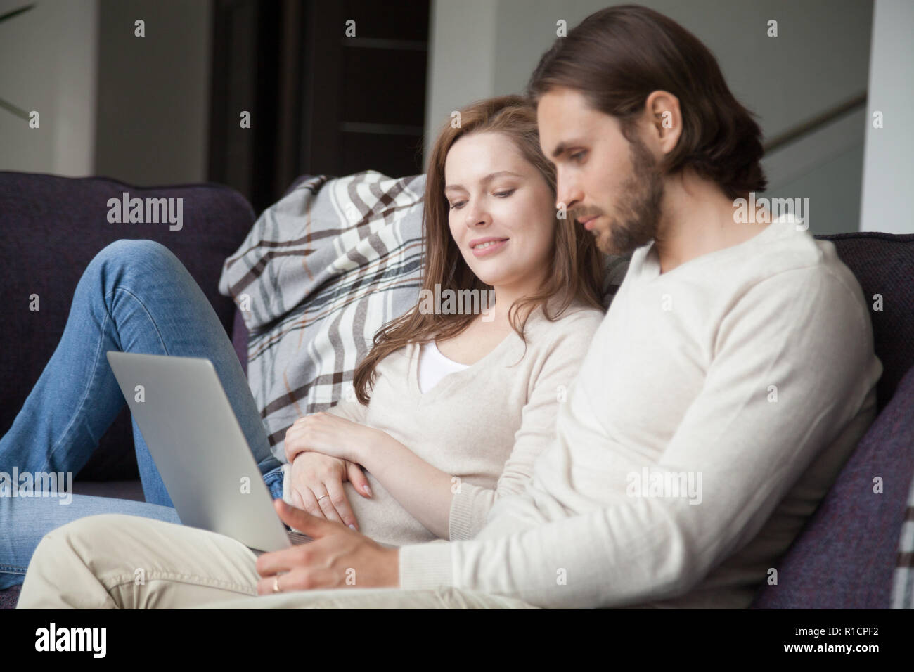 Couple sitting together on couch using laptop Stock Photo - Alamy