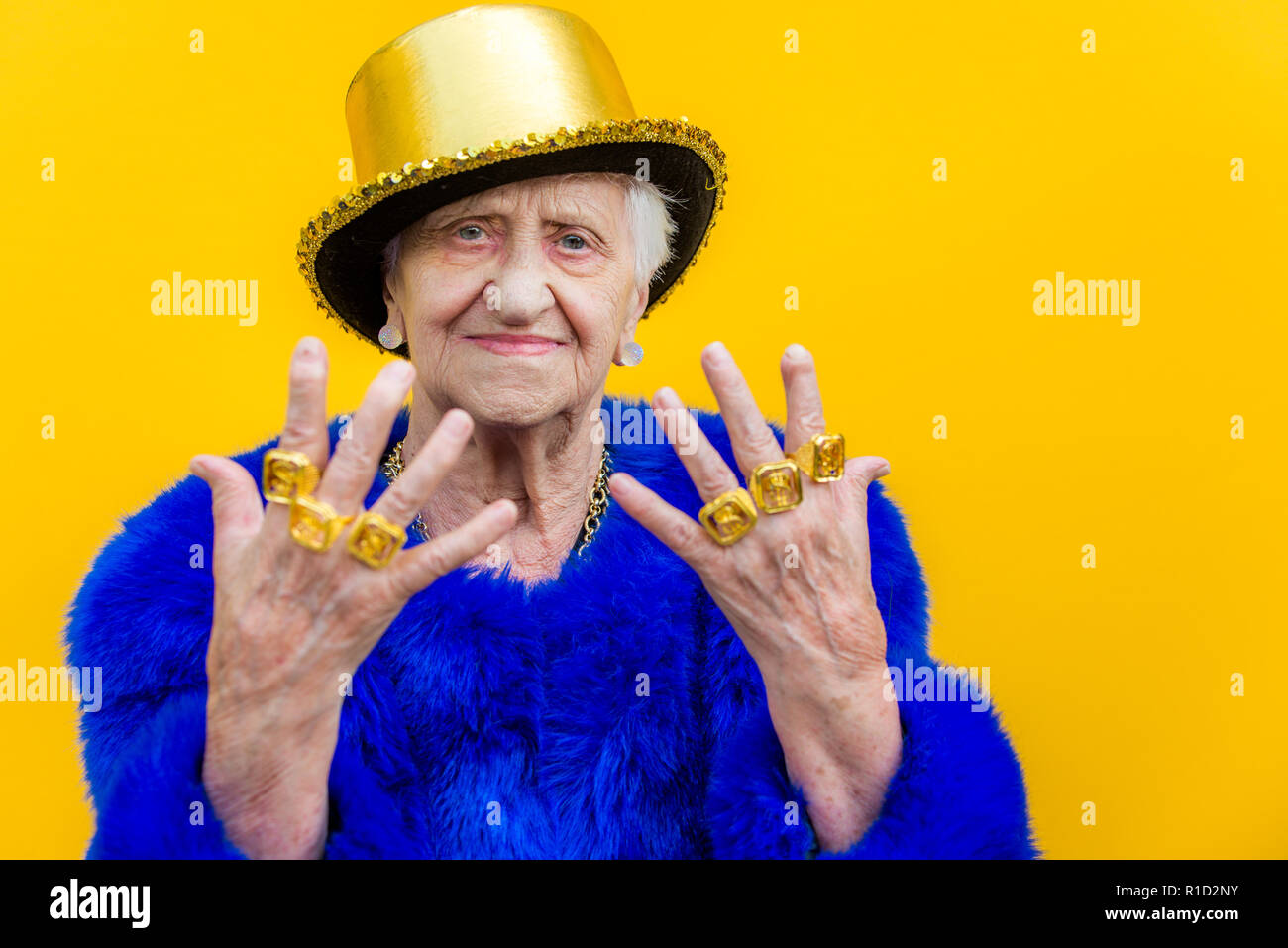 Funny and extravagant senior woman posing on colored background ...