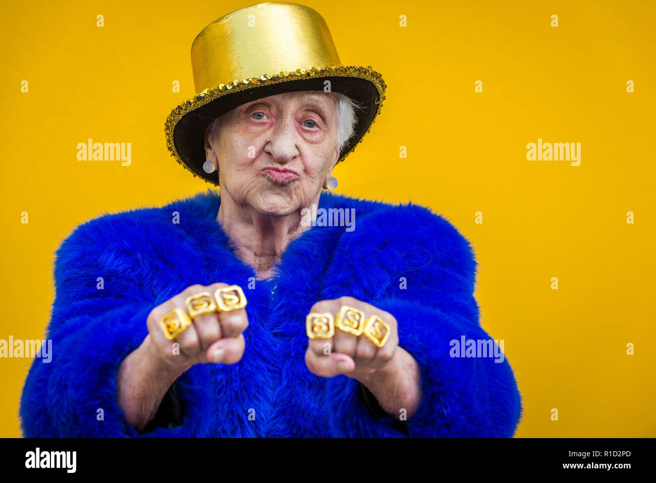 Funny and extravagant senior woman posing on colored background ...