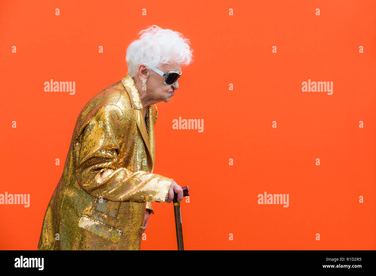Funny and extravagant senior woman posing on colored background ...
