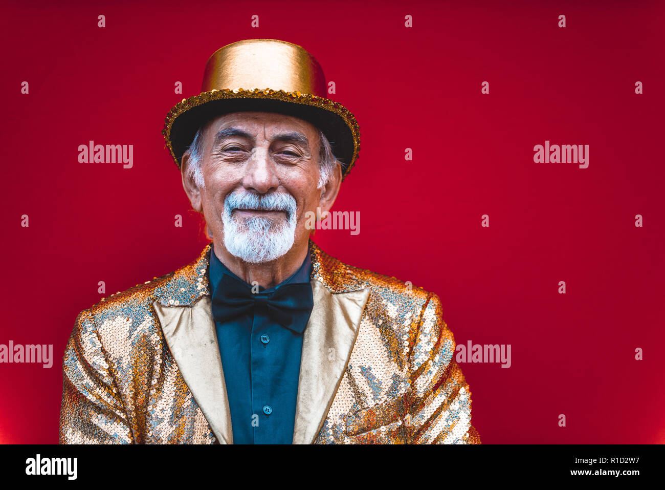 Funny and extravagant senior man posing on colored background ...