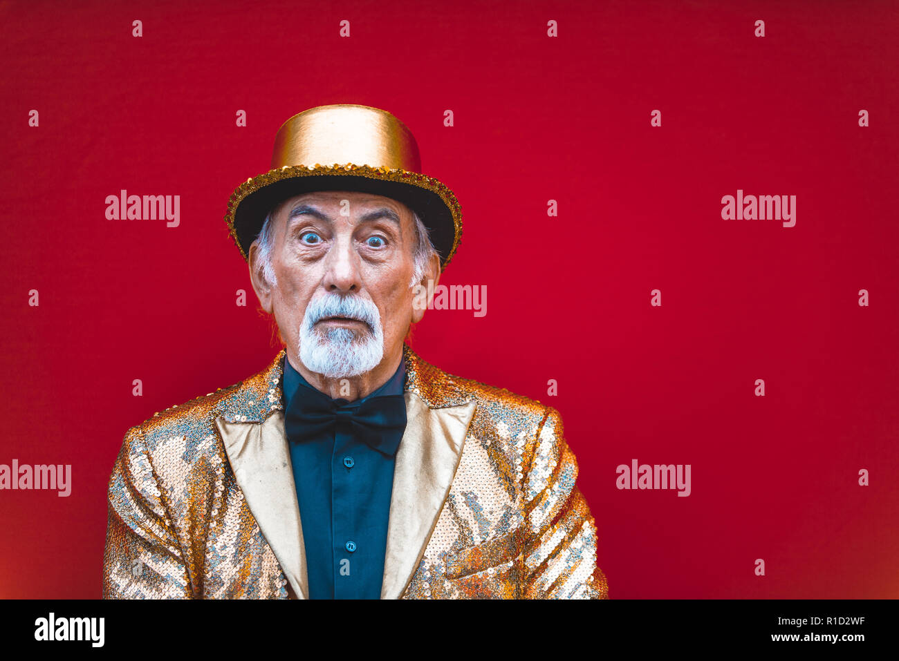 Funny and extravagant senior man posing on colored background ...