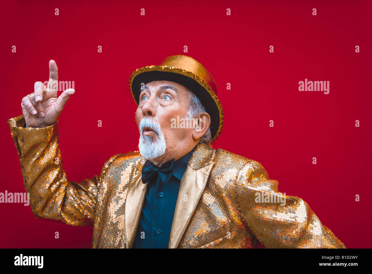 Funny and extravagant senior man posing on colored background ...