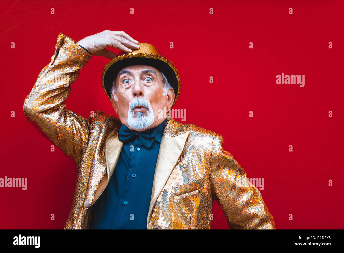 Funny and extravagant senior man posing on colored background ...