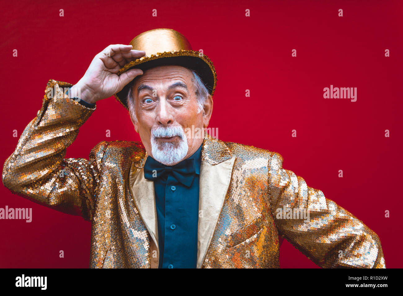 Funny and extravagant senior man posing on colored background ...