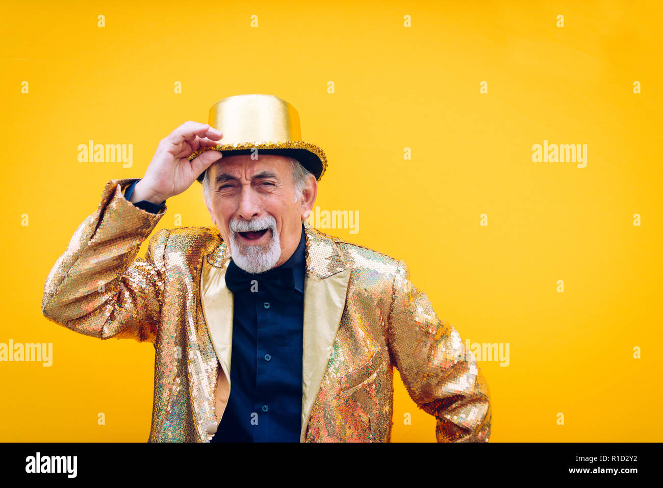 Funny and extravagant senior man posing on colored background ...