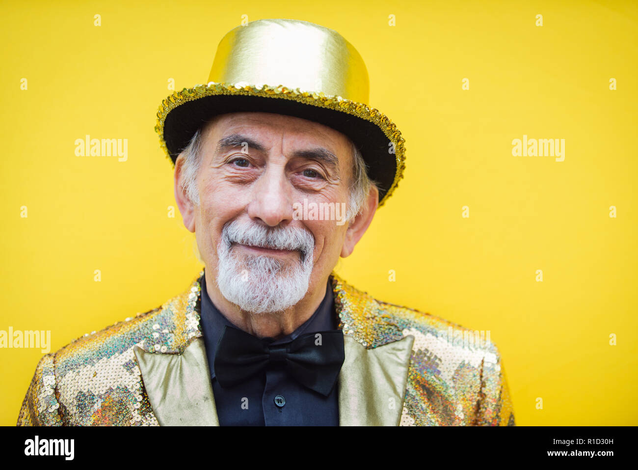 Funny and extravagant senior man posing on colored background ...