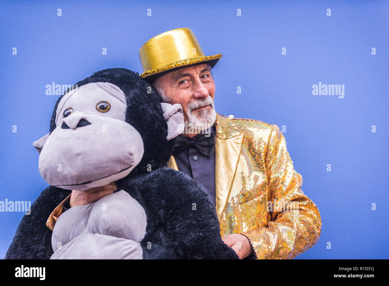 Funny and extravagant senior man posing on colored background ...
