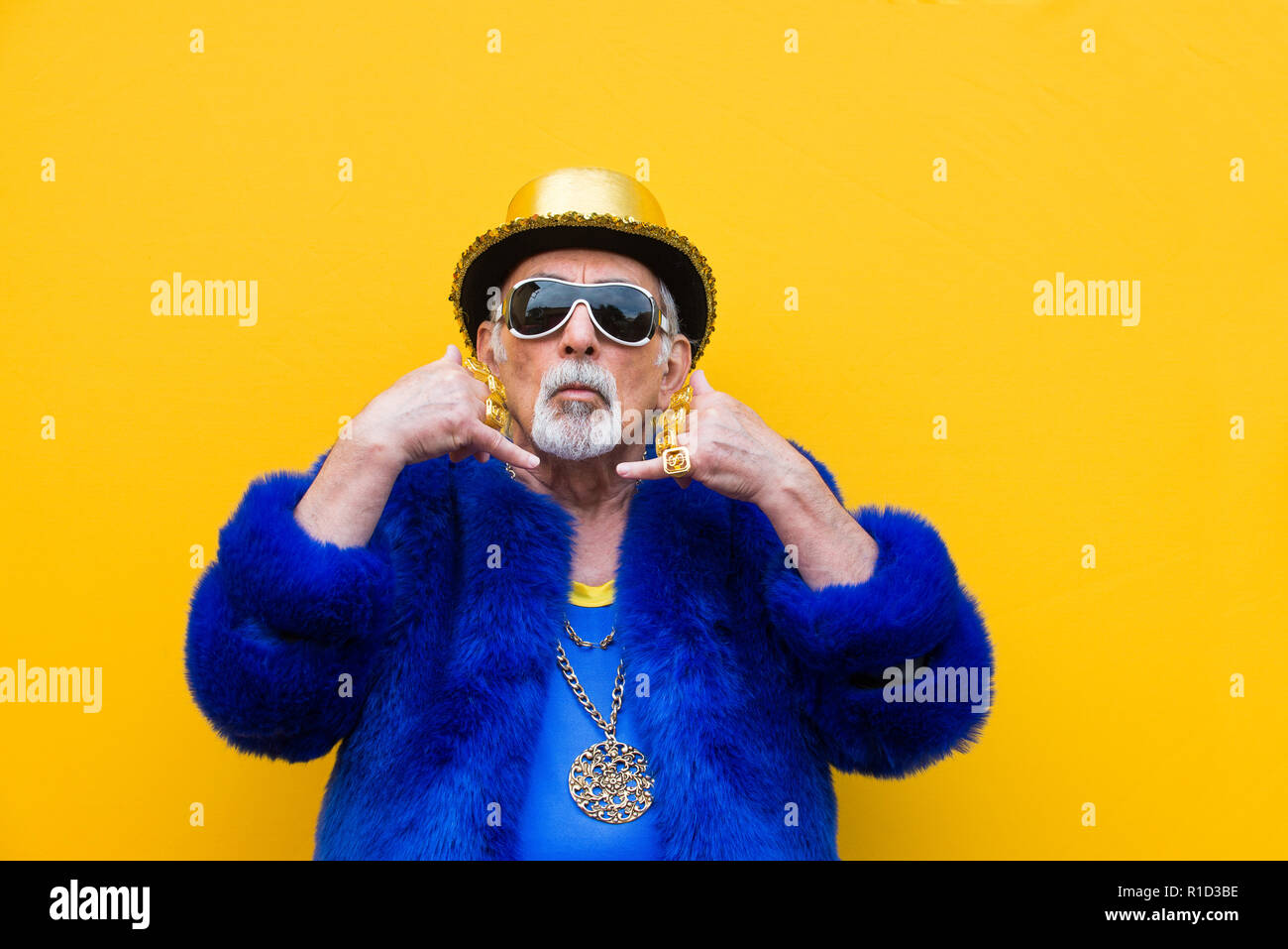 Funny and extravagant senior man posing on colored background ...