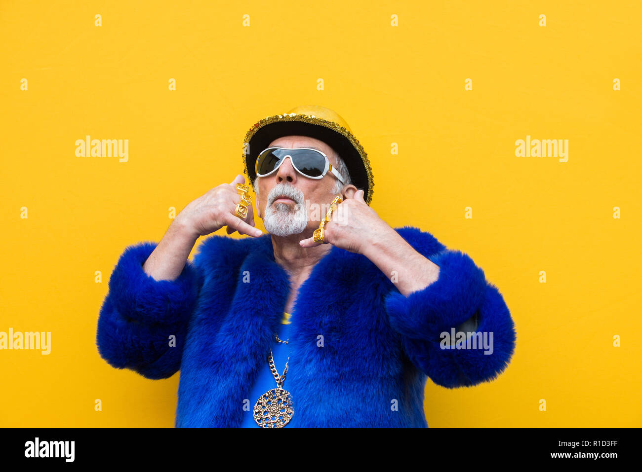Funny and extravagant senior man posing on colored background ...