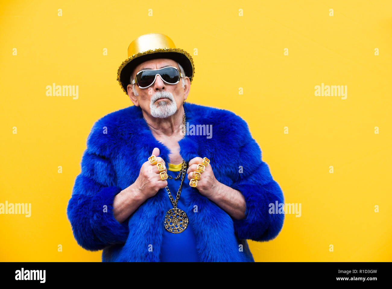 Funny and extravagant senior man posing on colored background ...