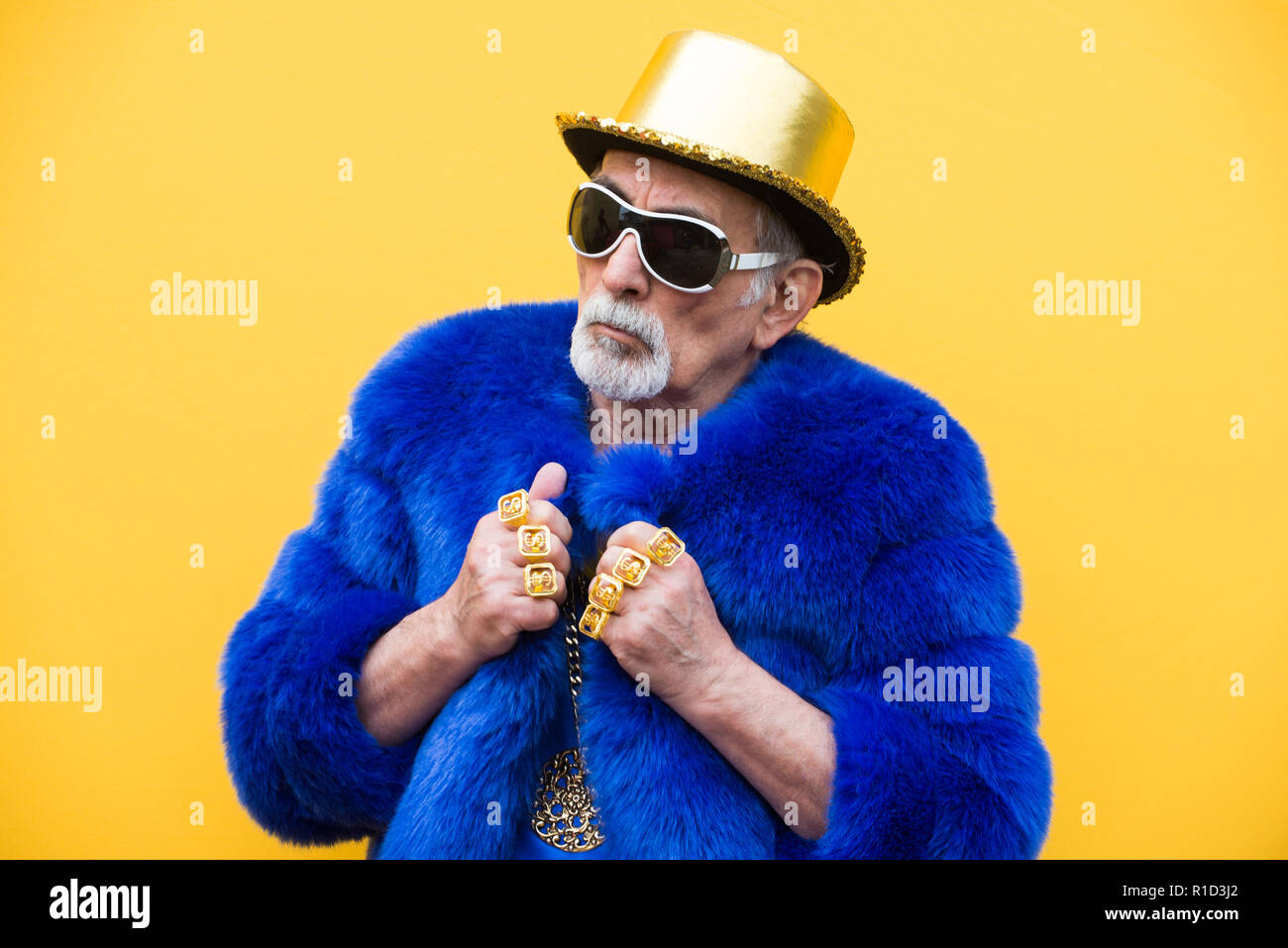 Funny and extravagant senior man posing on colored background ...