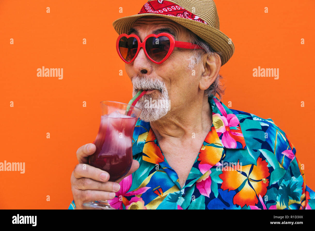 Funny and extravagant senior man posing on colored background ...