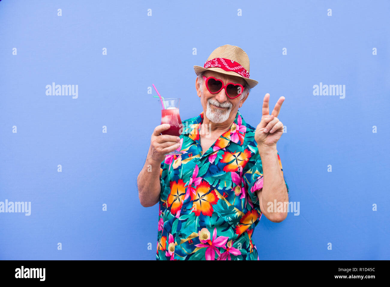 Funny and extravagant senior man posing on colored background ...