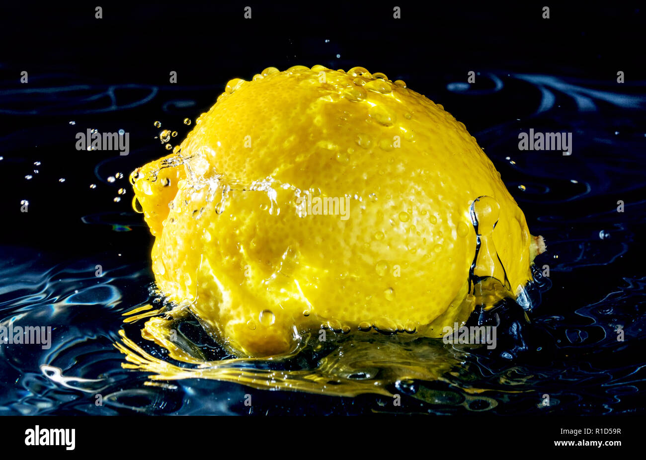 Lemon with splashes falling drops of water close-up macro on black ...