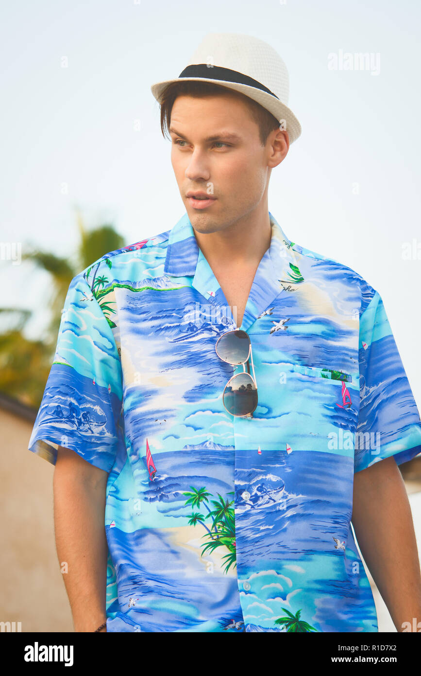 A handsome male model posing in Summer shirt outdoor against a blue sky ...