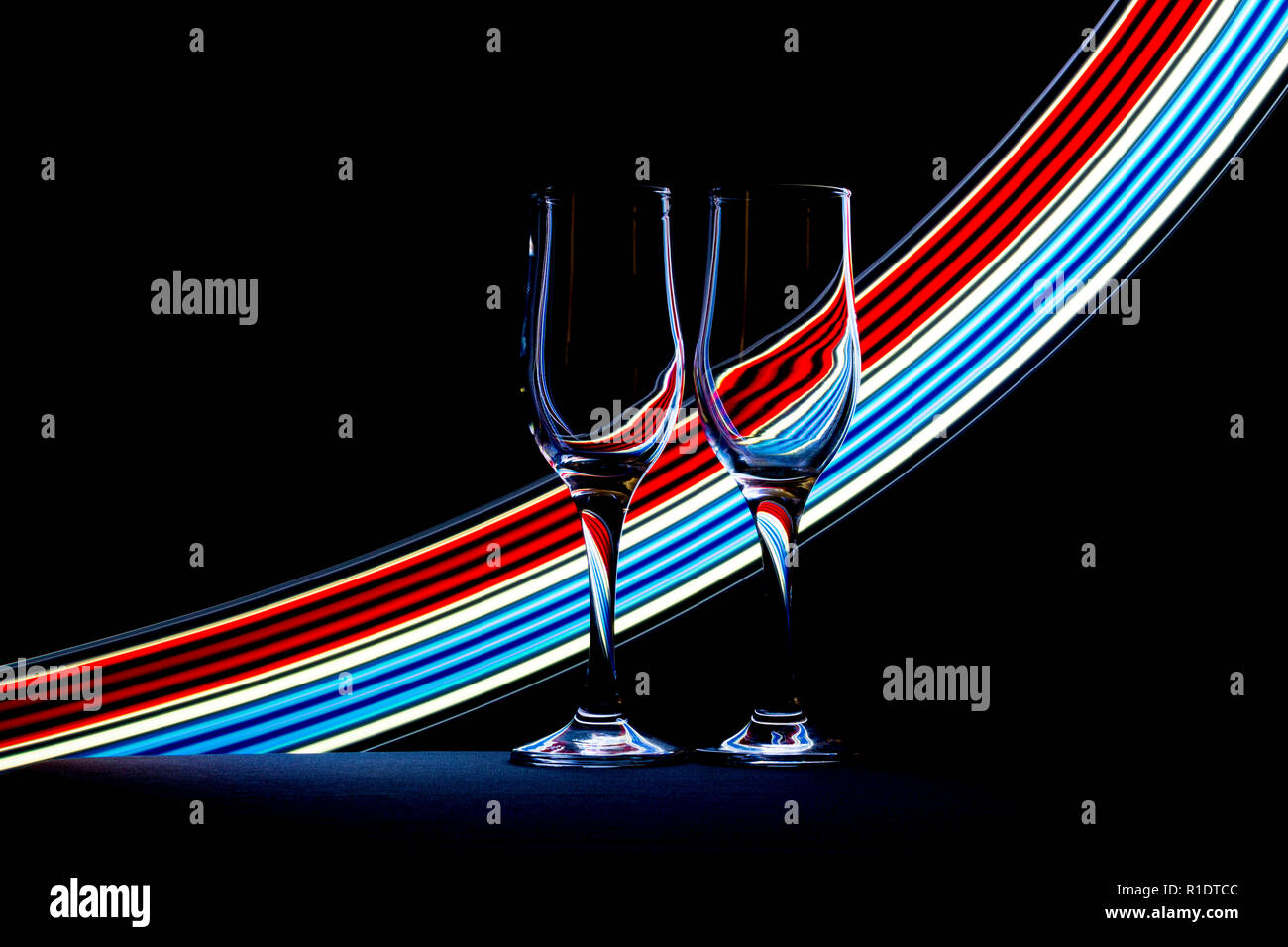 Two champagne glasses with streaks of multicoloured neon light behind ...